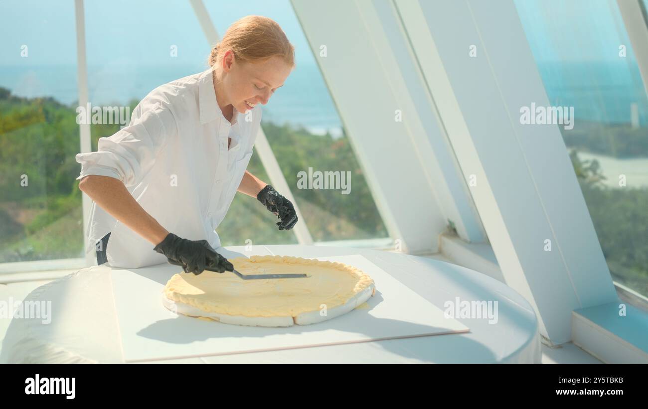 Young red haired female pastry chef assembling cake Pavlova in banquet ...