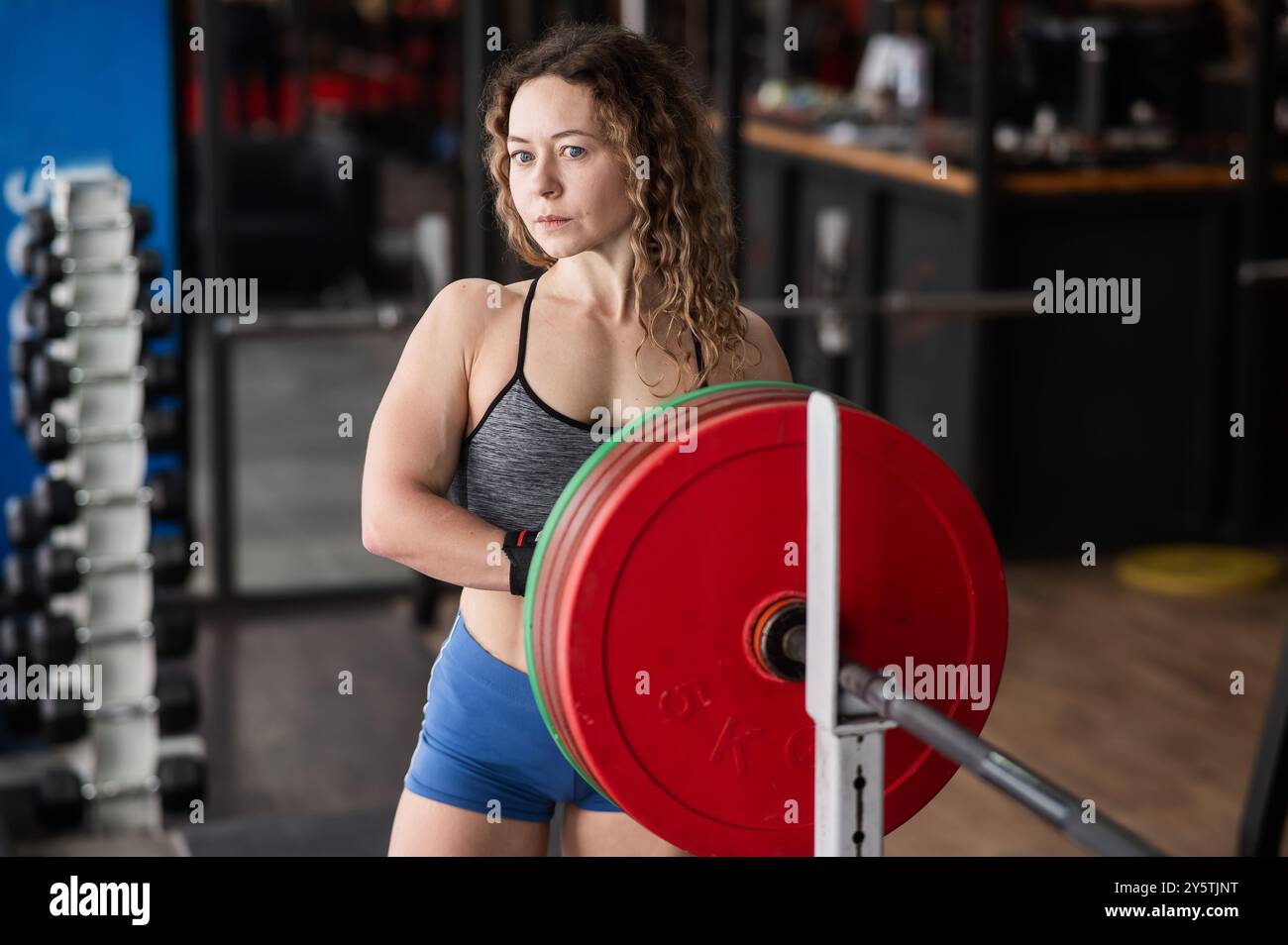 Caucasian forty year old woman putting a weight plate on a barbell in ...