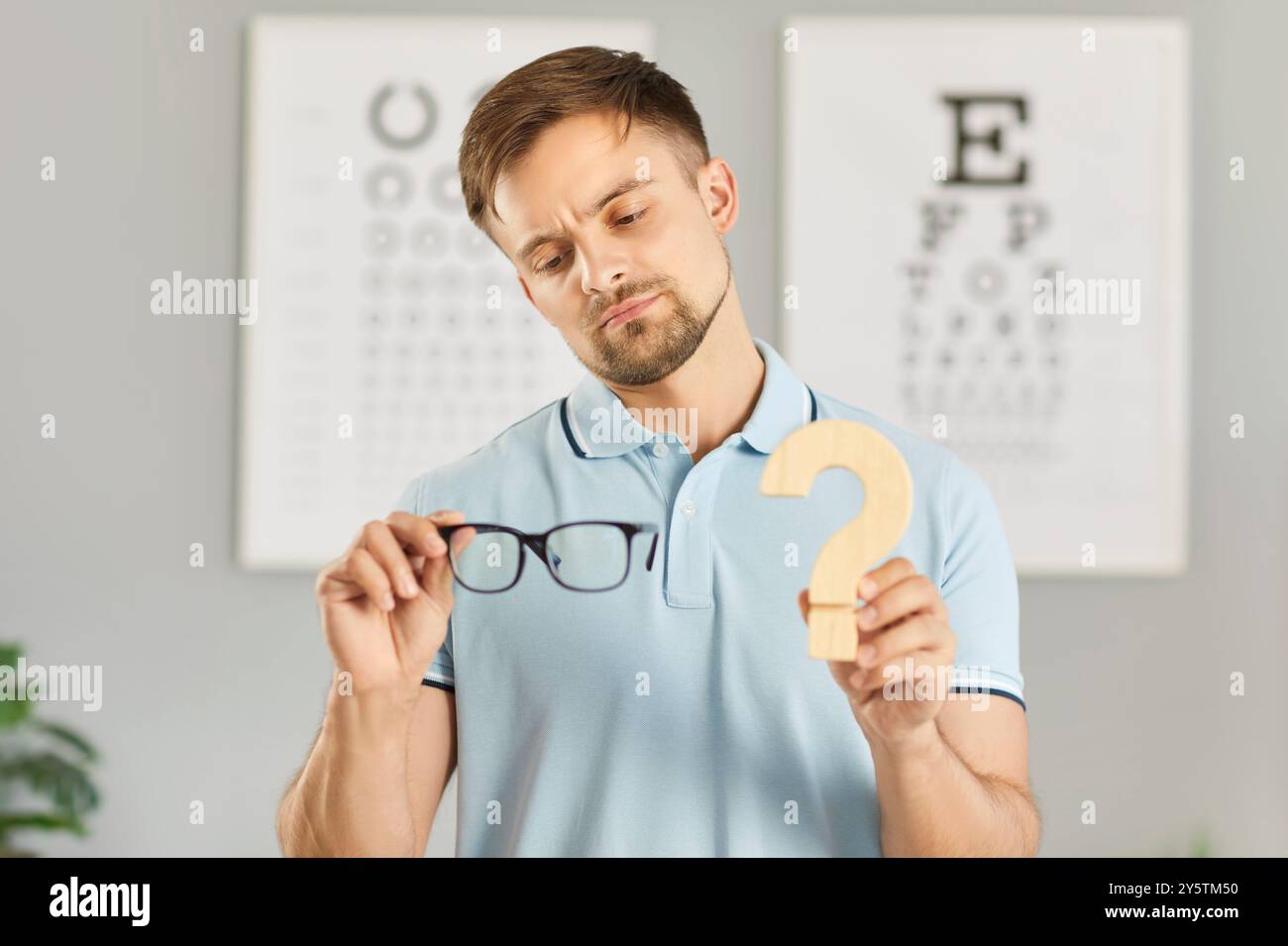 Young male patient holding eyeglasses and question mark choosing ...