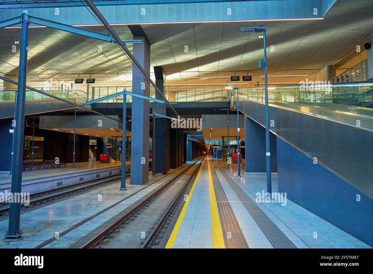 Modern train station platform with escalators and empty railway tracks. Architecture of ...