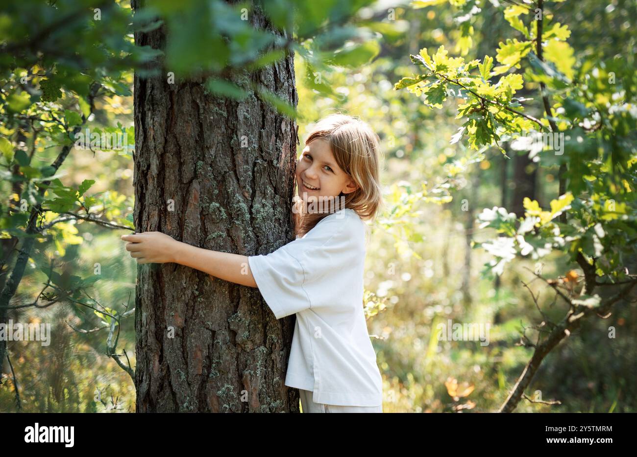 A teenage girl hugs a tree in the forest. Hugging and touching trees to ...