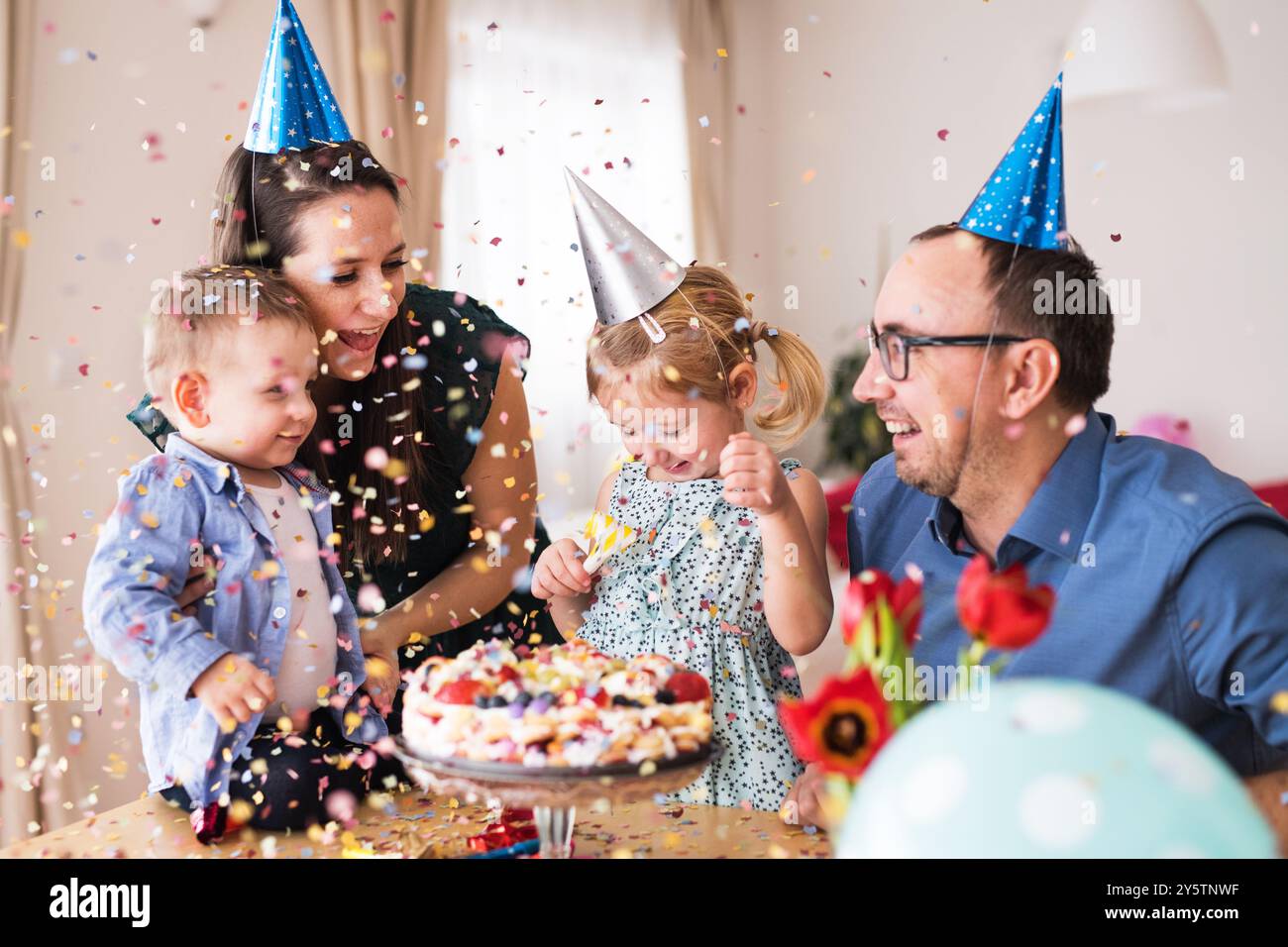 Birthday party with confetti and birthday cake. Parents and two kids ...