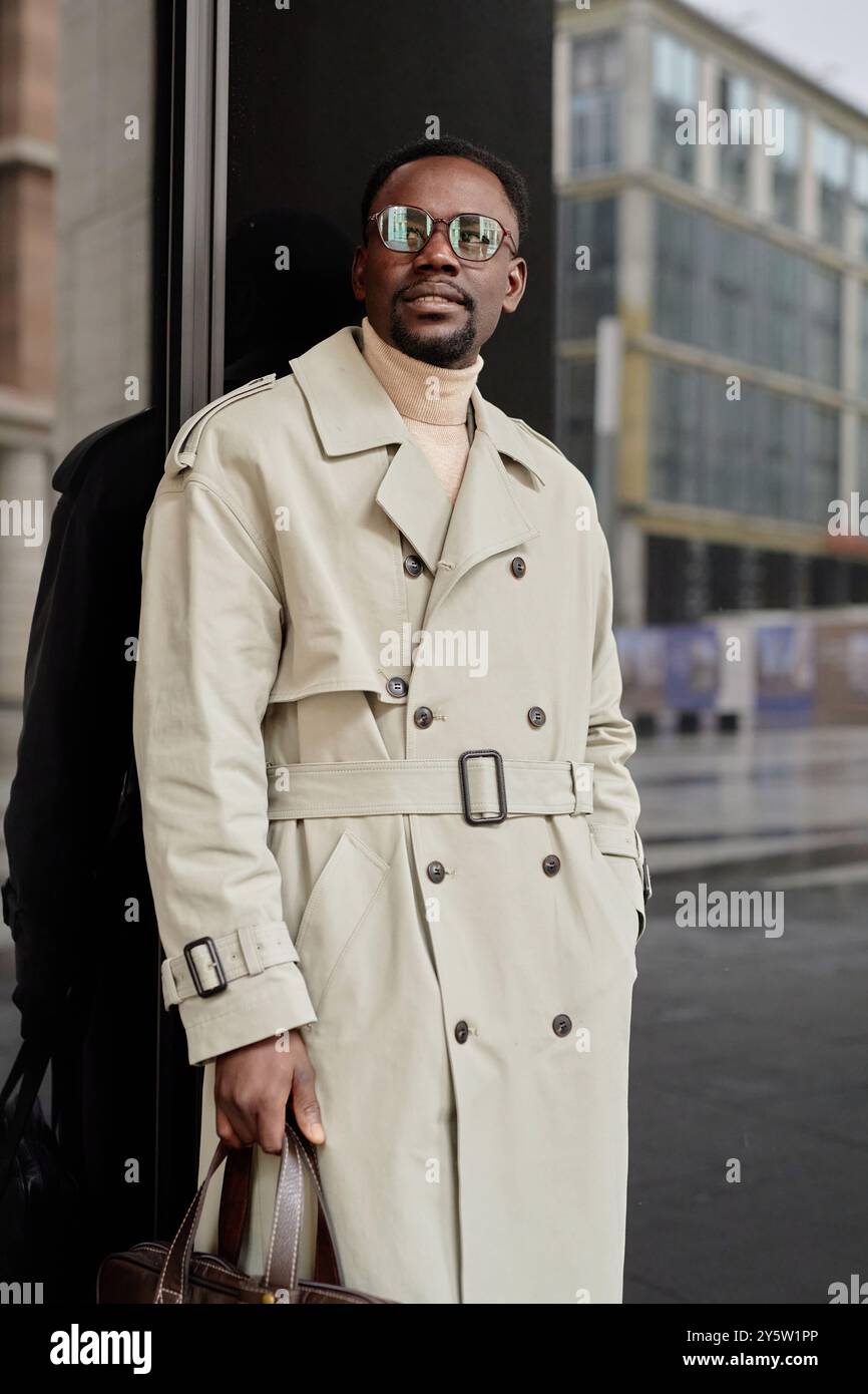 Portrait of stylish man standing outside modern building, holding a ...