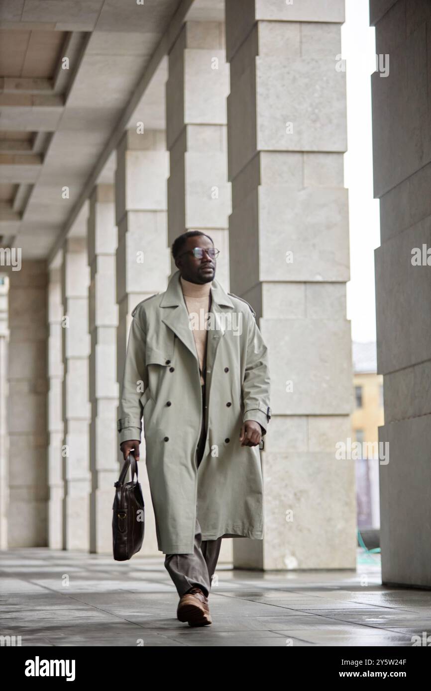 Man in trench coat walking through modern building corridor carrying ...