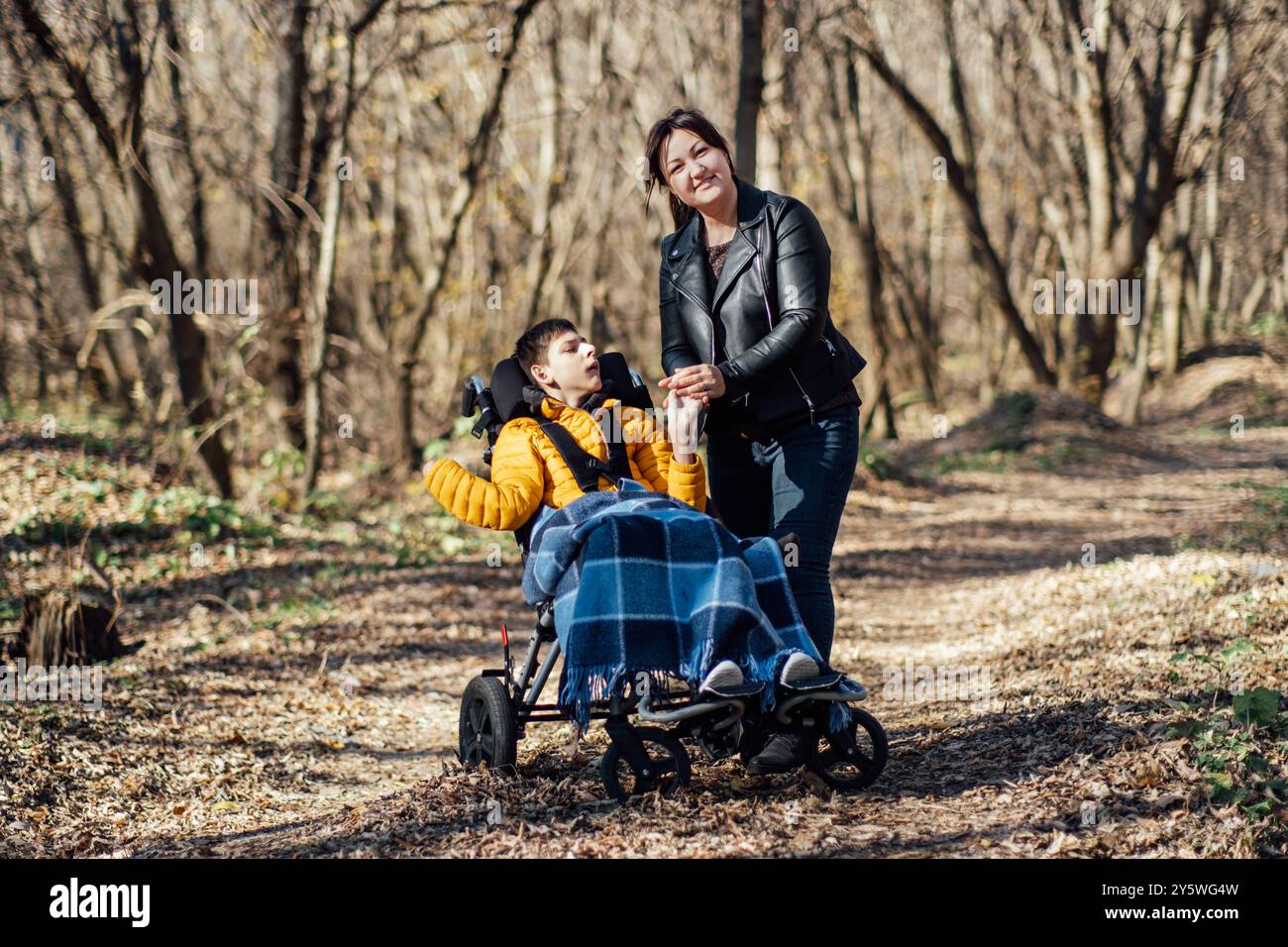 Mother supporting child in wheelchair during nature walk in forest ...