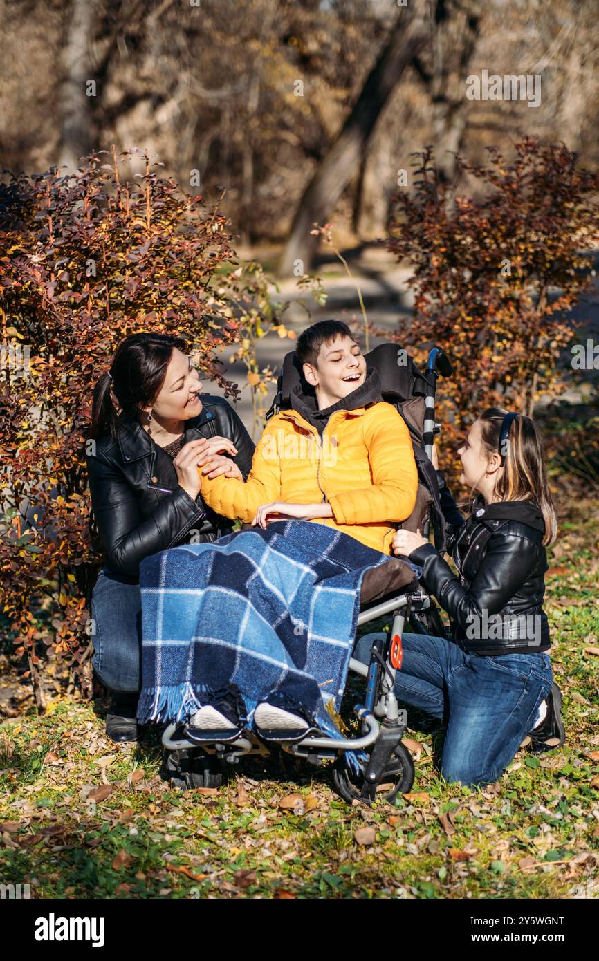 Mother and sibling bonding with child in wheelchair during outdoor time ...
