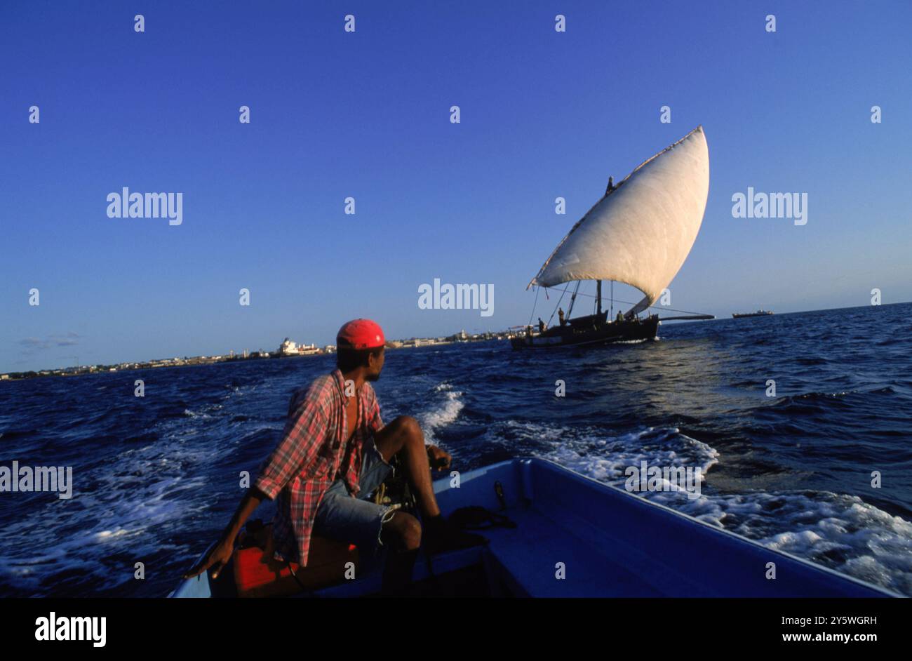 Swahili man in motorboat, freight dhow in background, Zanzibar ...