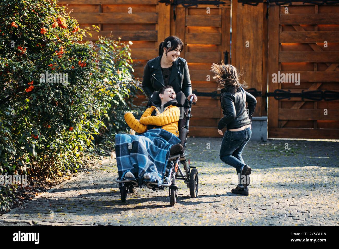Mother and sibling bonding with child in wheelchair during outdoor time ...