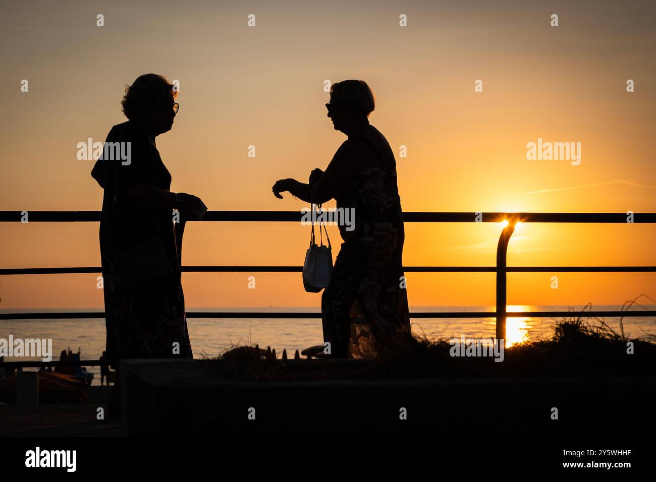 silhouette of two old ladies talking at ocean sunset. socializing ...