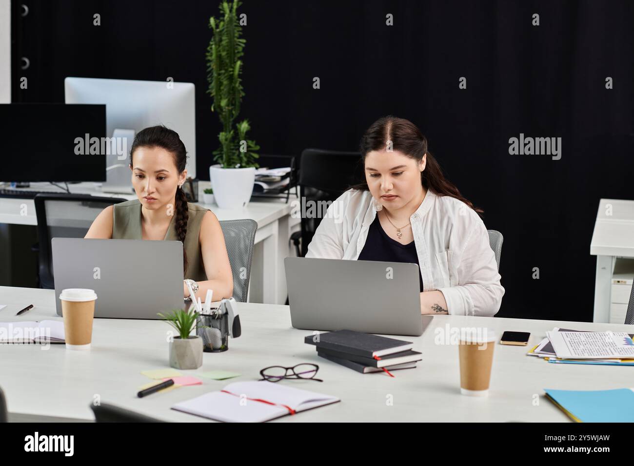 Two professional women focus intently on their laptops while seated at ...