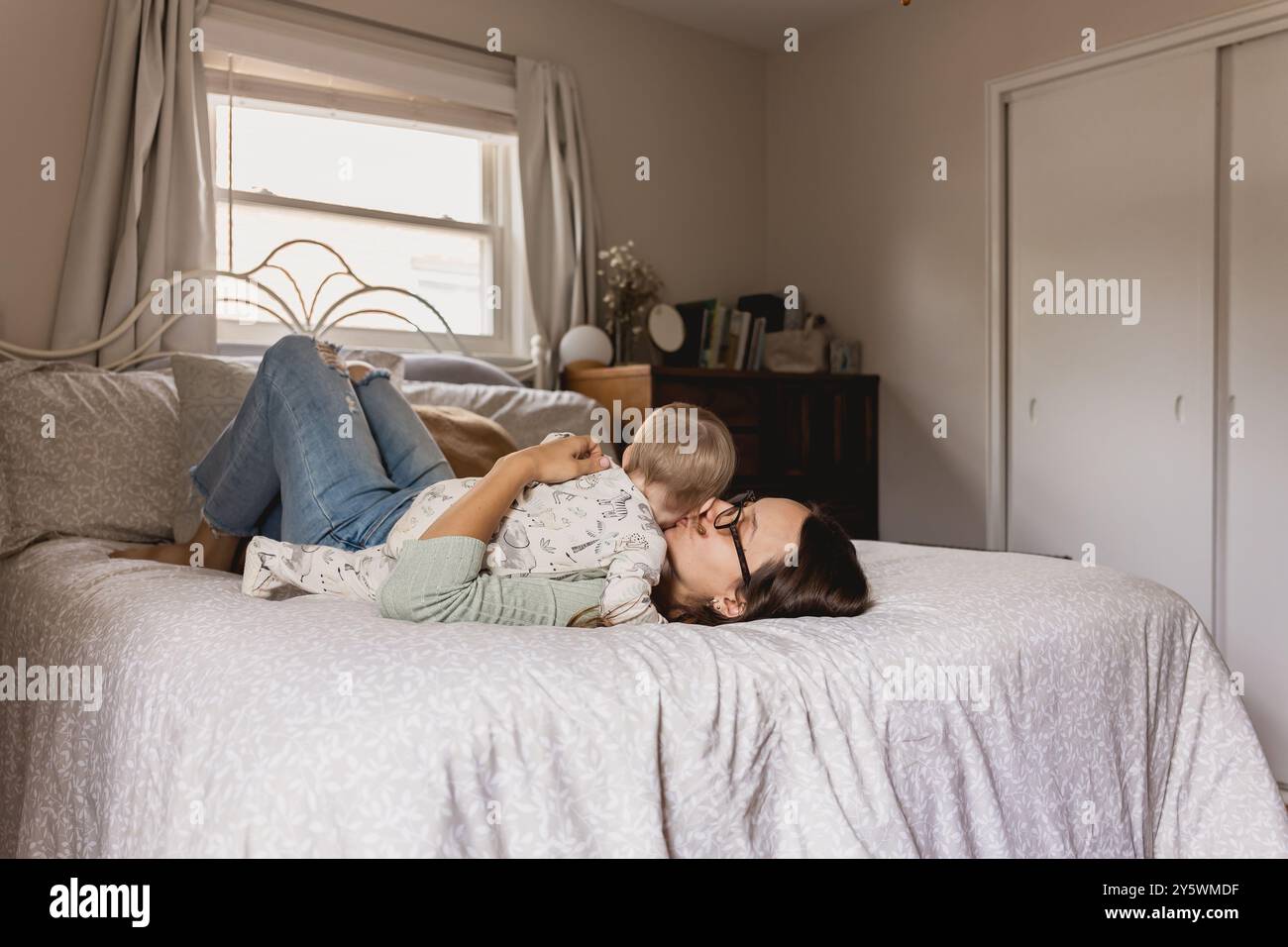 Mother lying on a bed, cuddling her baby in a peaceful bedroom Stock ...