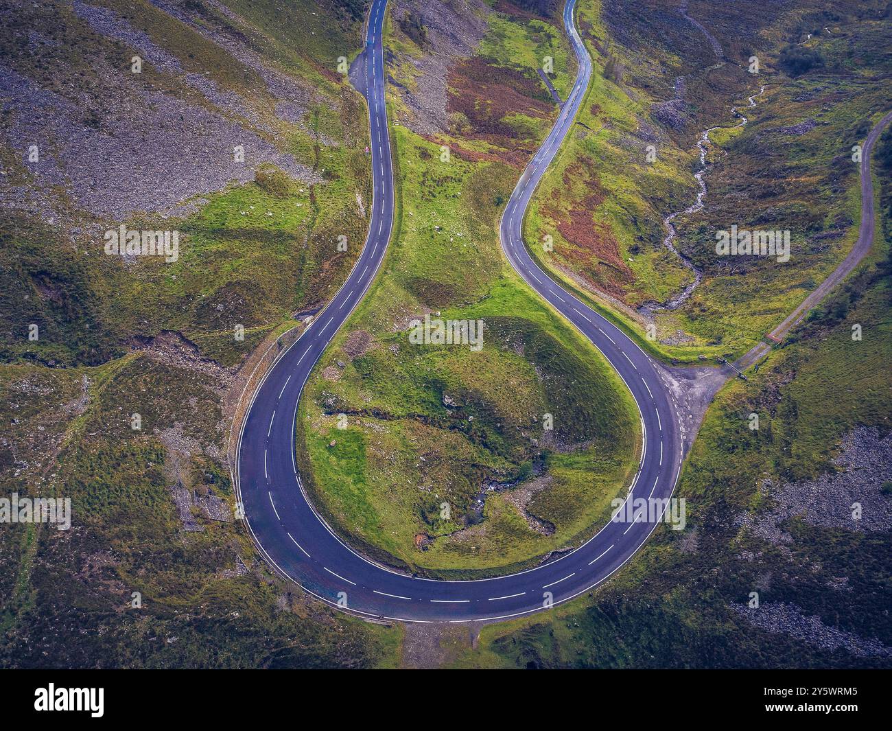 A winding mountain road curves through lush green hills, creating a ...