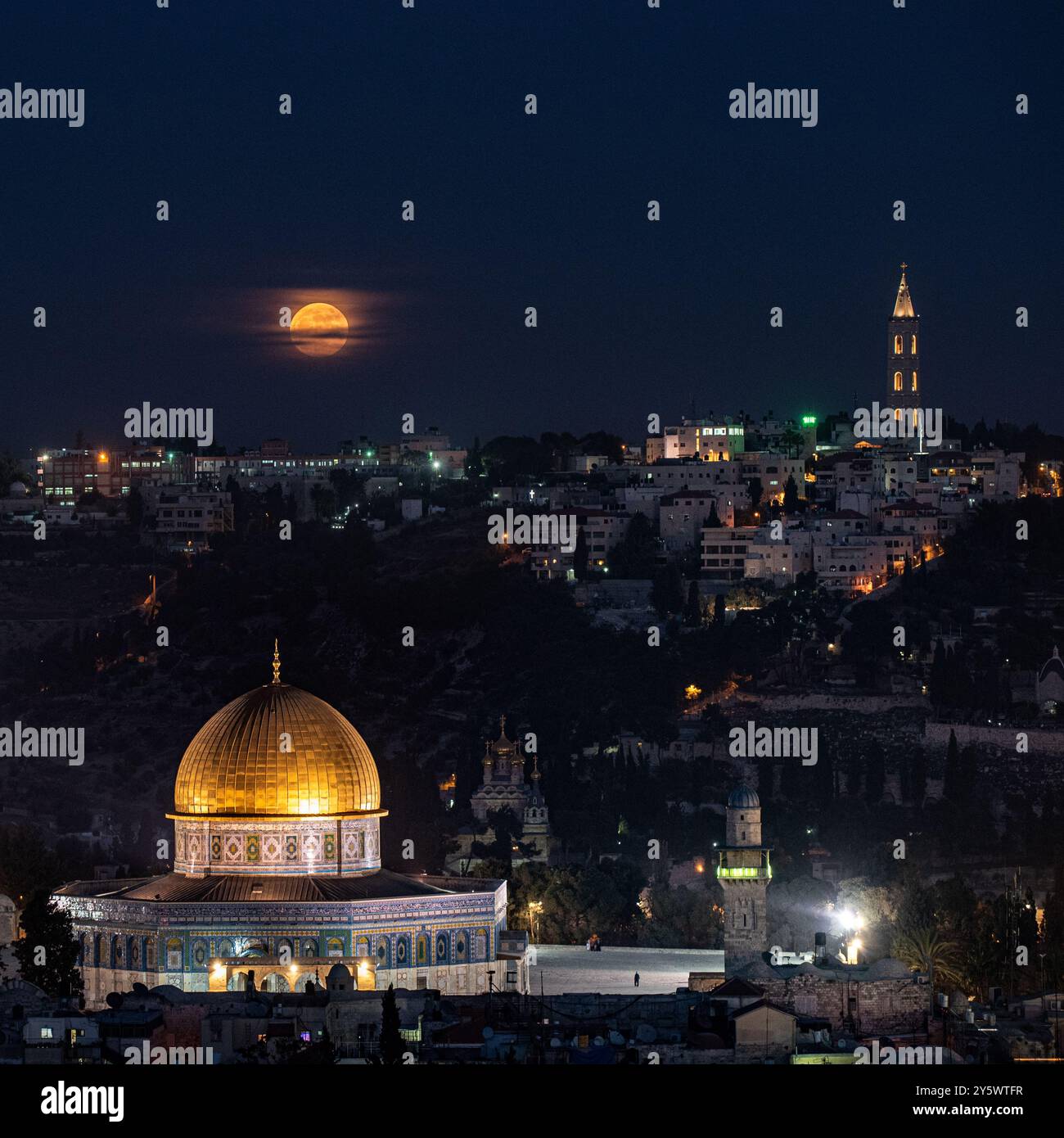 A full, orange moon rises low on the horizon over Mount Scopus, the ...