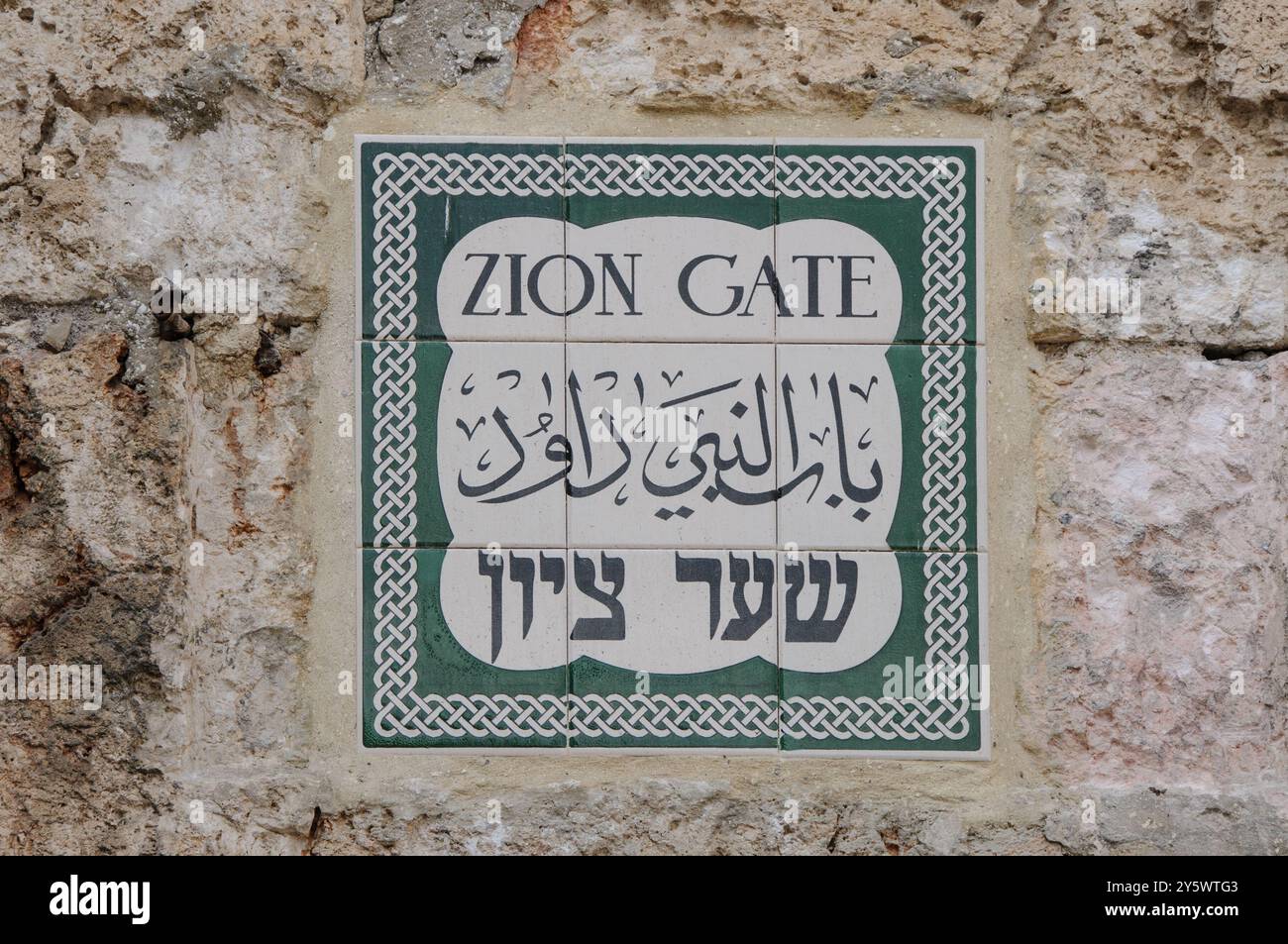 A ceramic tile street sign on an old stone wall in Hebrew, Arabic and ...