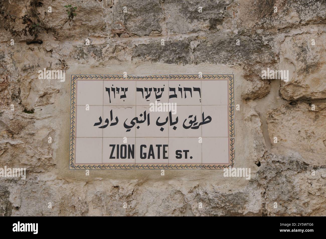A ceramic tile street sign on an old stone wall in Hebrew, Arabic and ...