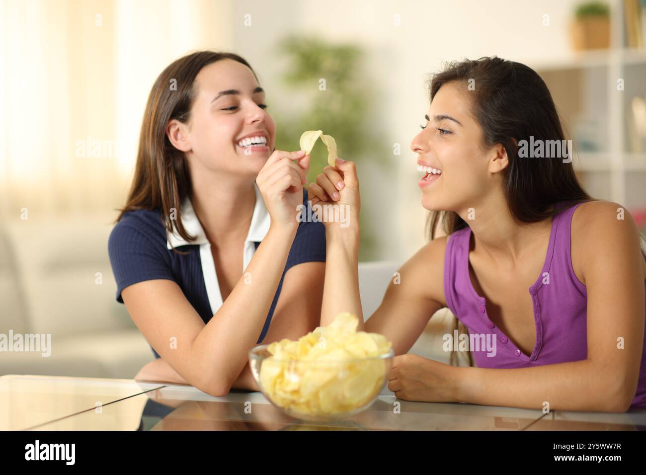 Happy friends eating toasting with potato chips at home Stock Photo - Alamy