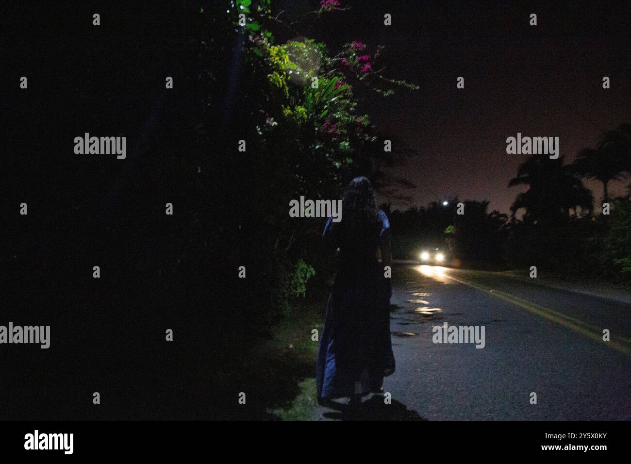 woman walking alone at night with oncoming vehicle headlights ...