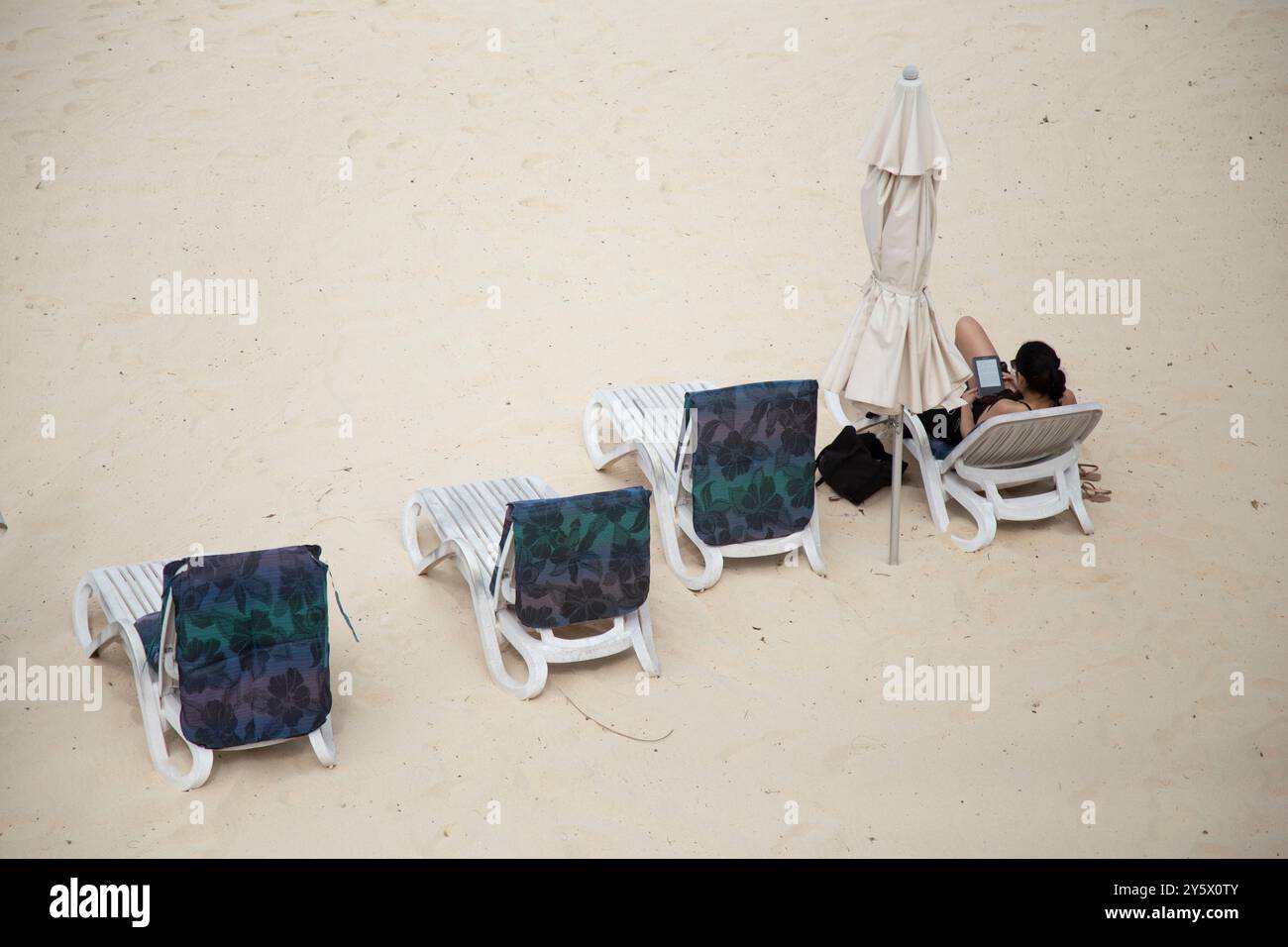 Aerial view of a sandy beach with a person relaxing on a sun lounger ...