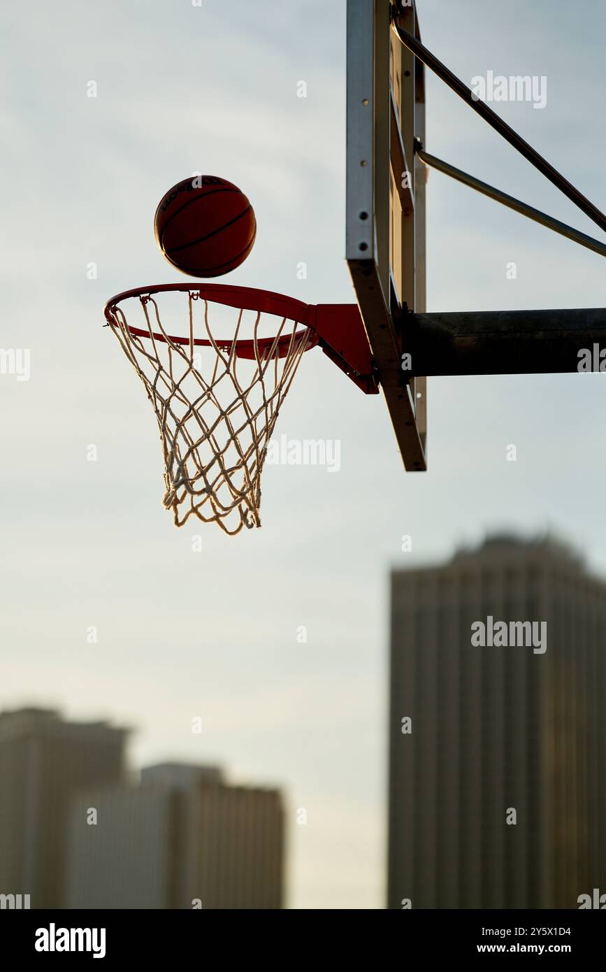 Basketball approaching the hoop against an early evening sky backdrop ...