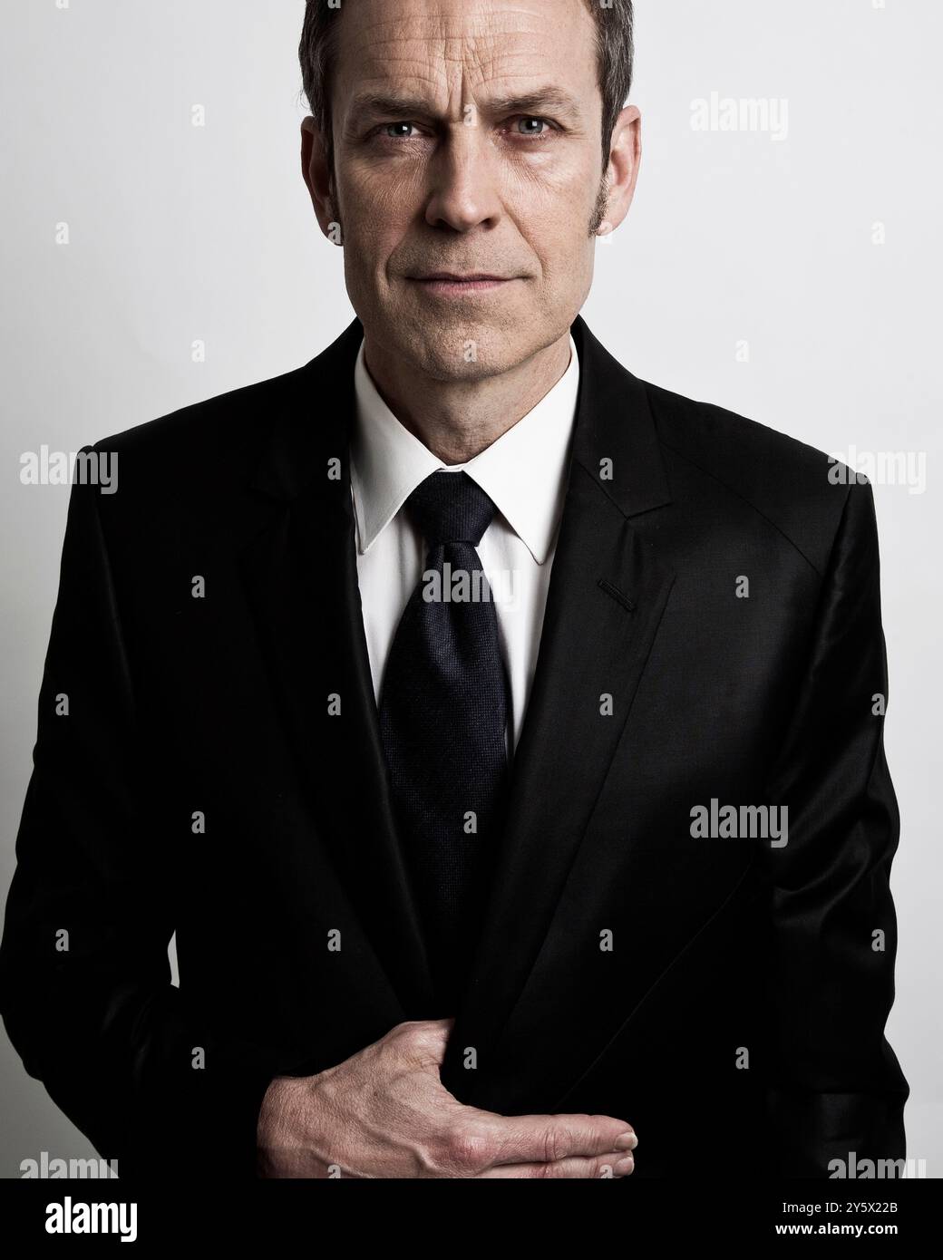 Professional man in a black suit and tie posing with a confident stance ...