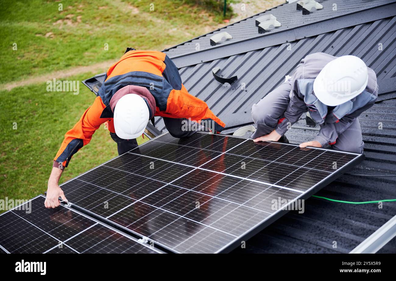 Installers installing photovoltaic solar panels on roof of house. Men ...