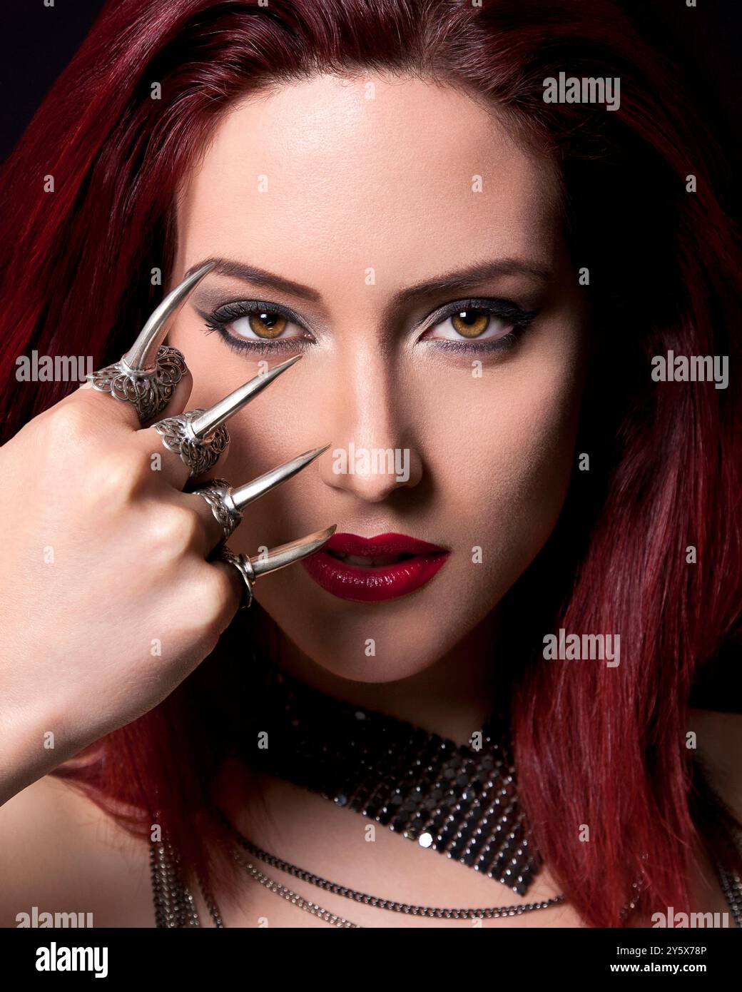 Red-haired woman with striking makeup wearing claw rings and looking at ...