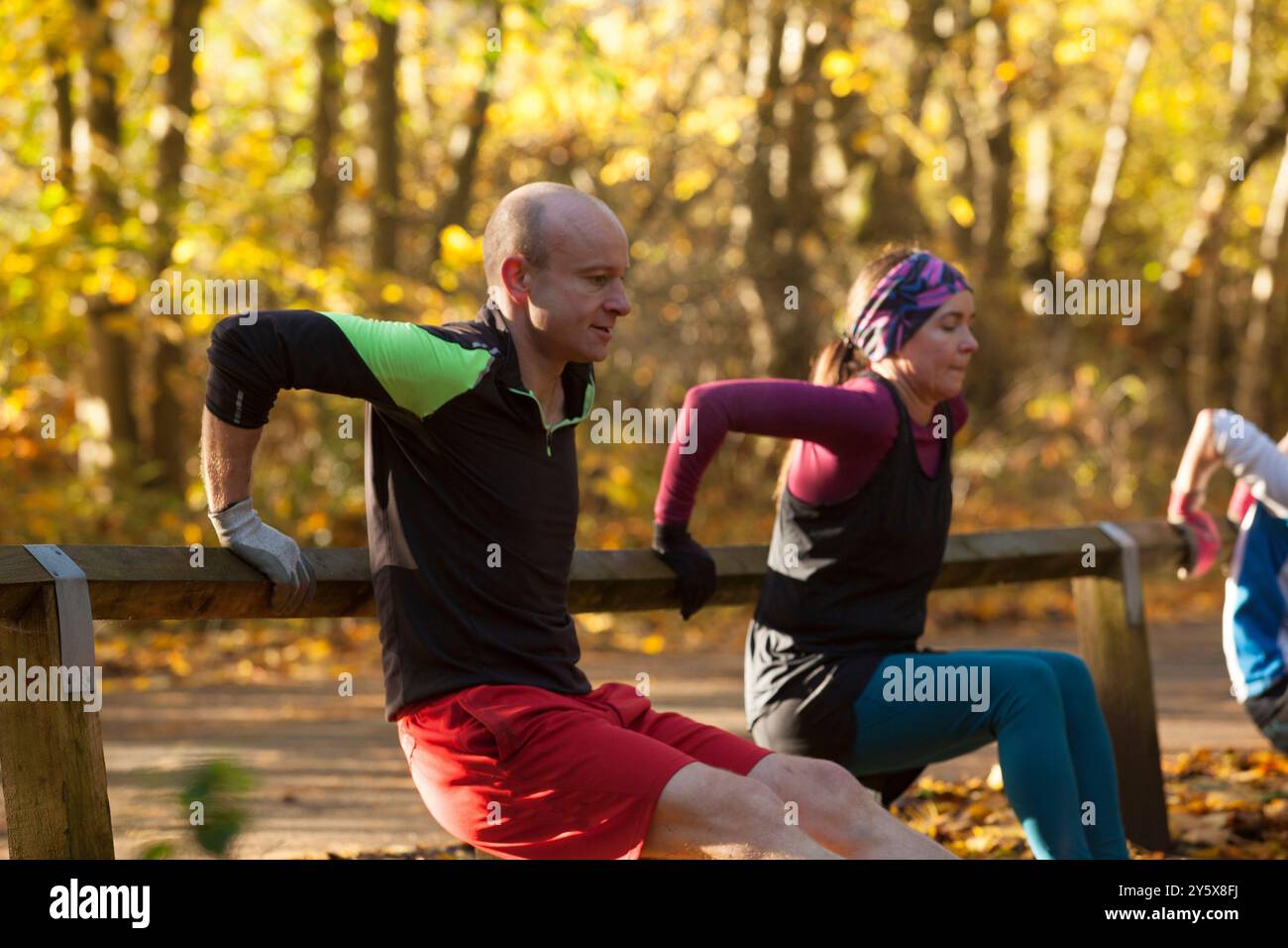 Group of people performing tricep dips on wooden railings in an autumn ...