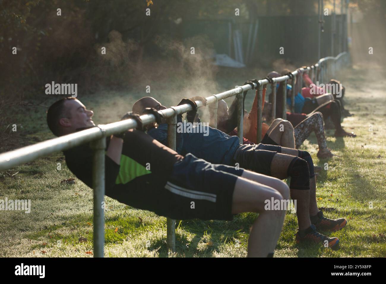 Group of people performing outdoor pull-up exercises on a row of bars ...
