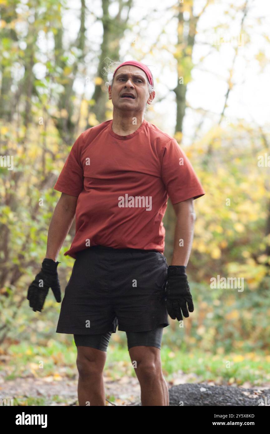 Mature man catching his breath during a run in a wooded area, dressed ...