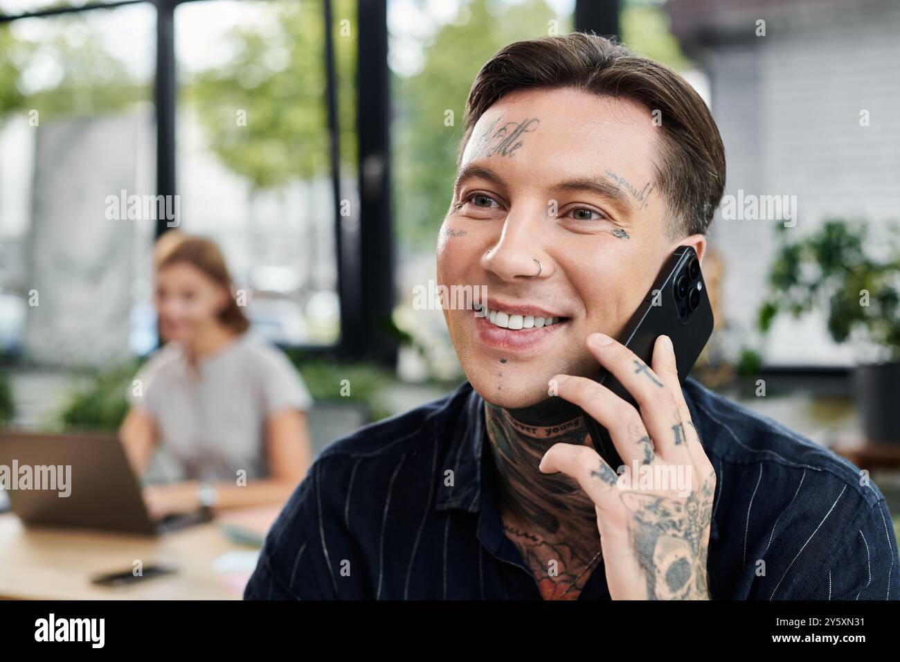 A young coworker enjoys a lively phone call while smiling in a modern ...