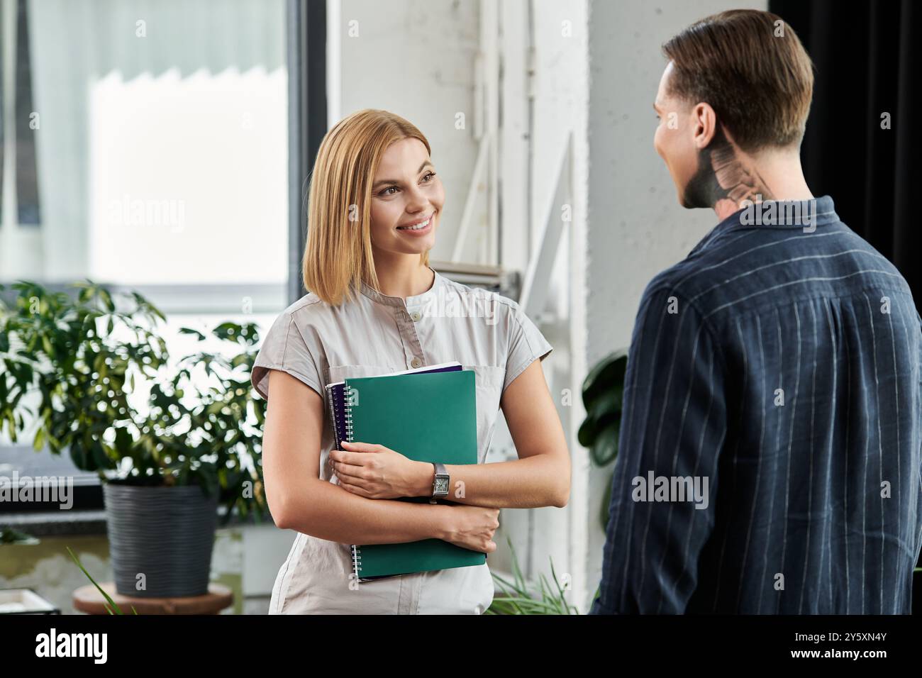 Two young professionals smile and share ideas, enhancing collaboration in a vibrant workplace ...