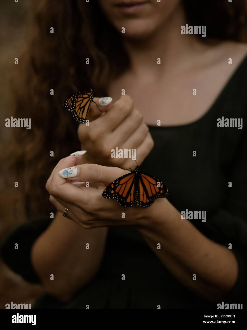 A woman with long brown hair holding two monarch butterflies in her ...