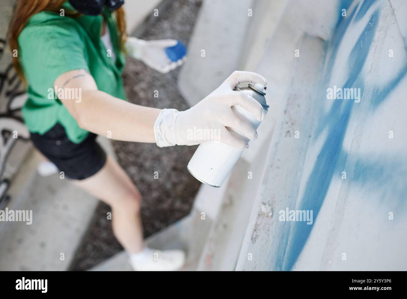 Person using spray paint to create graffiti art on urban wall, wearing ...