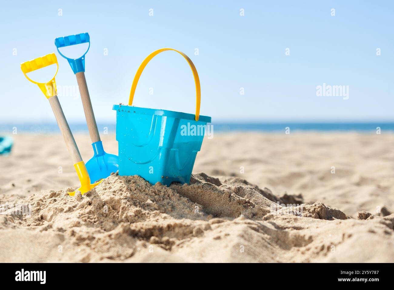 Blue and yellow toy bucket and shovels on a mound of sand on a sunny ...
