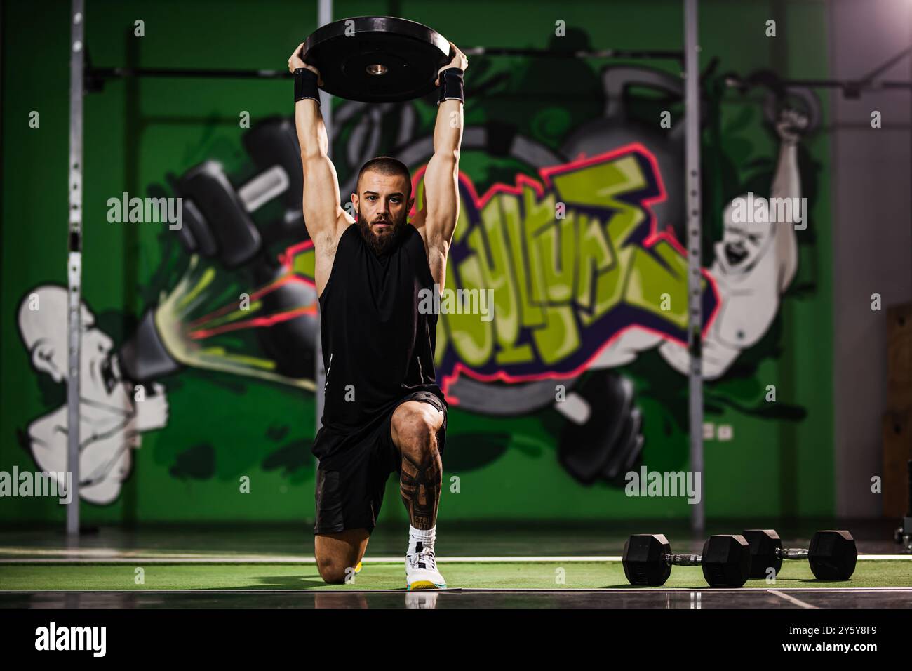 A determined male athlete performs a weightlifting exercise in a gym ...