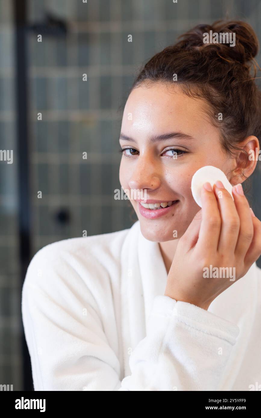 Applying facial toner, woman in white robe enjoying skincare routine ...