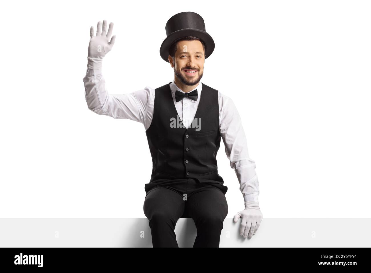 Magician sitting on a blank panel and waving isolated on white ...