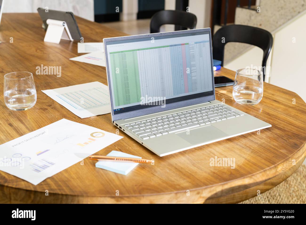Laptop displaying spreadsheet on wooden table with documents and water ...