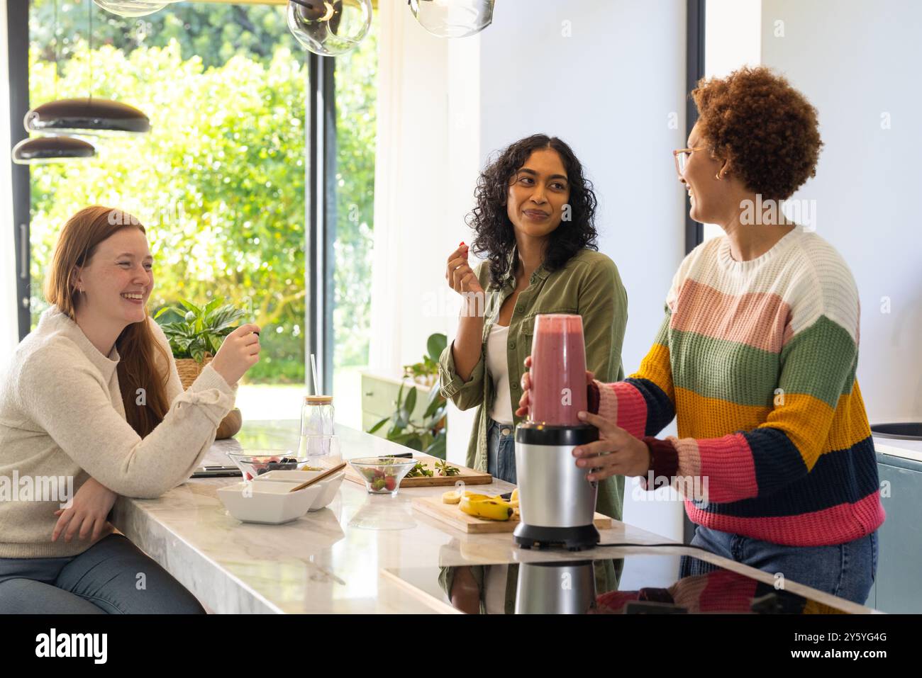 Making smoothies, diverse friends enjoying conversation in modern ...