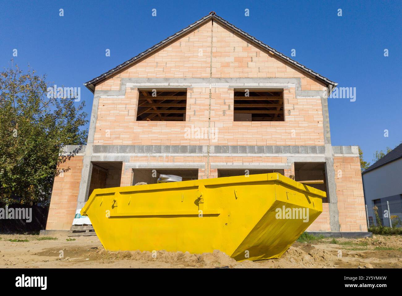 Unfinished brick house with yellow construction skip for waste disposal ...