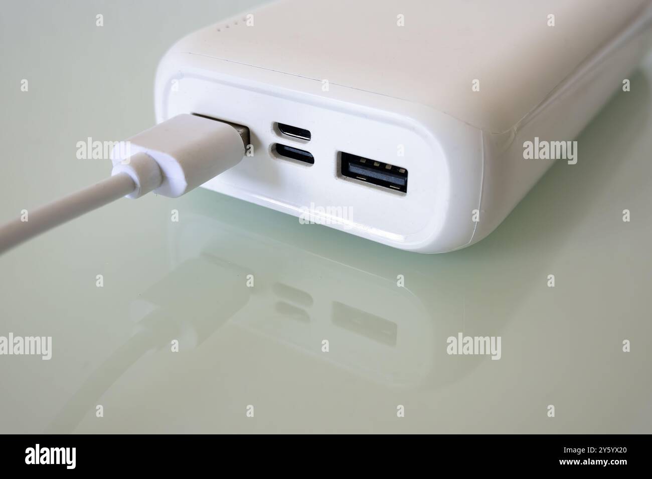 White power bank connected to a USB cable on a reflective glass ...