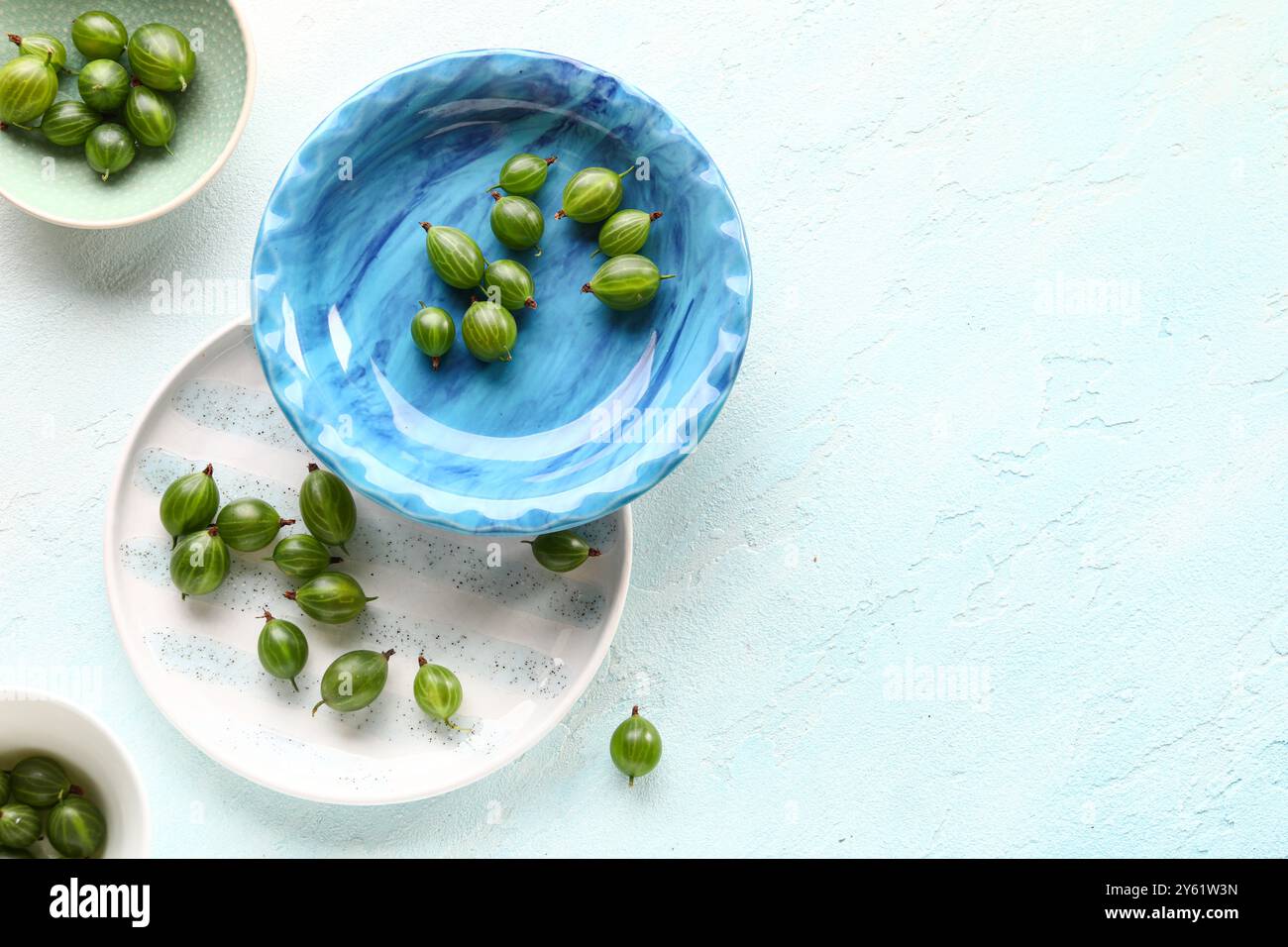Plates and bowls with fresh gooseberries on light blue background Stock ...