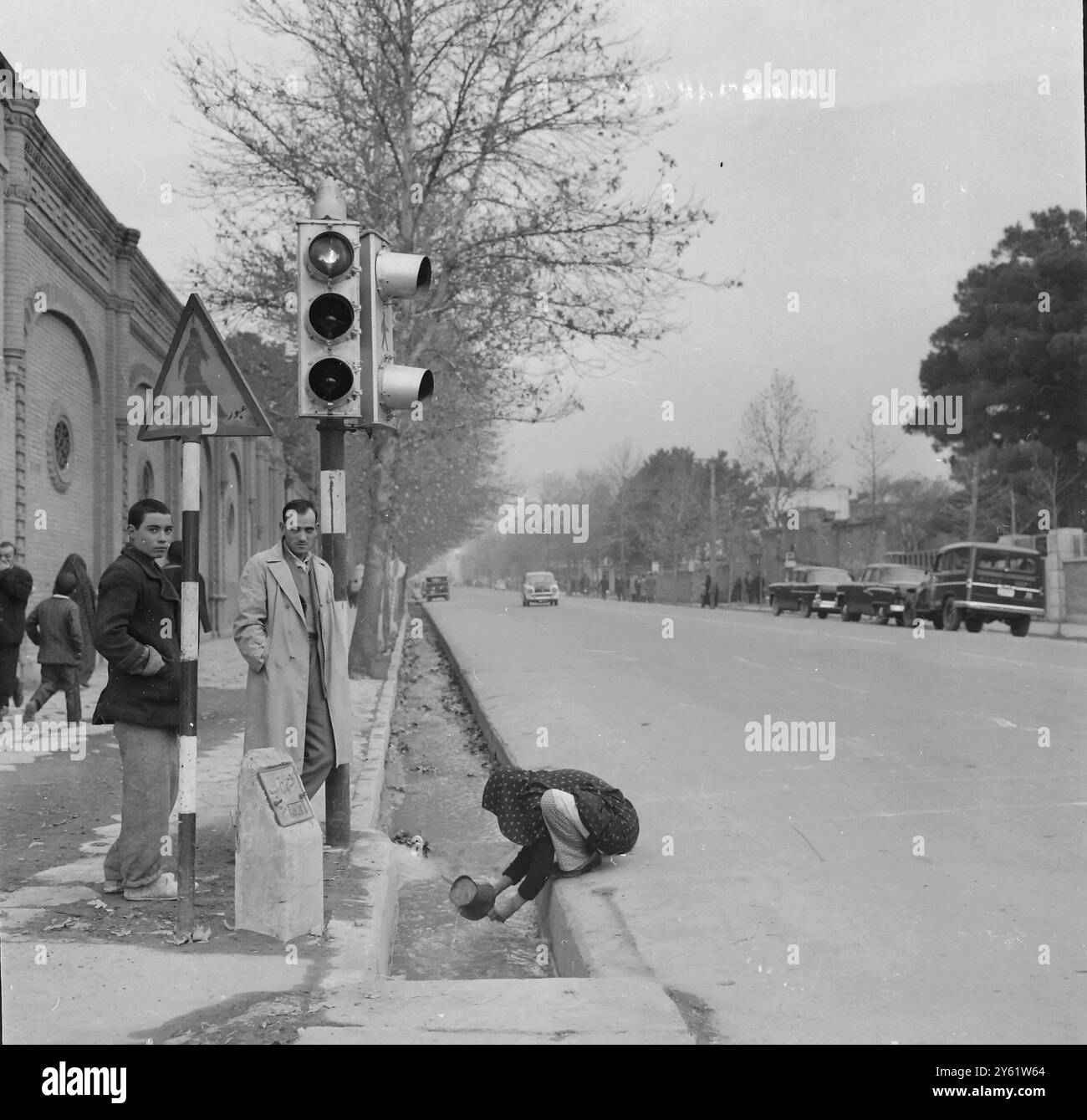A YOUNG IRANIAN WASHES A POT IN A DRAIN THAT RUNS DOWN THE STREET ...
