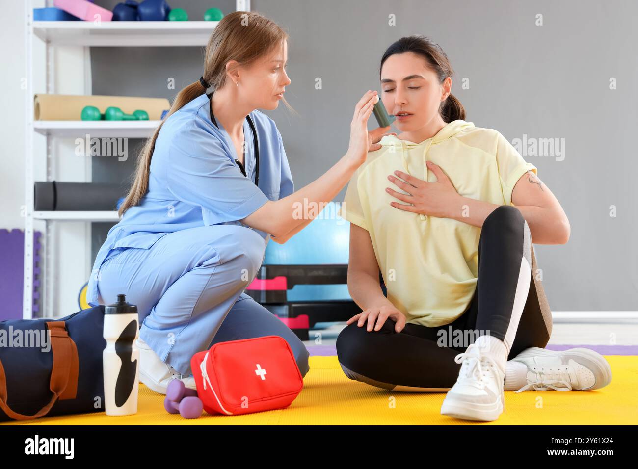 Female doctor with inhaler giving young woman first aid in gym Stock ...