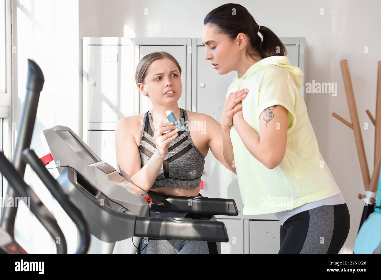 Female trainer giving inhaler to woman with asthma attack on treadmill ...