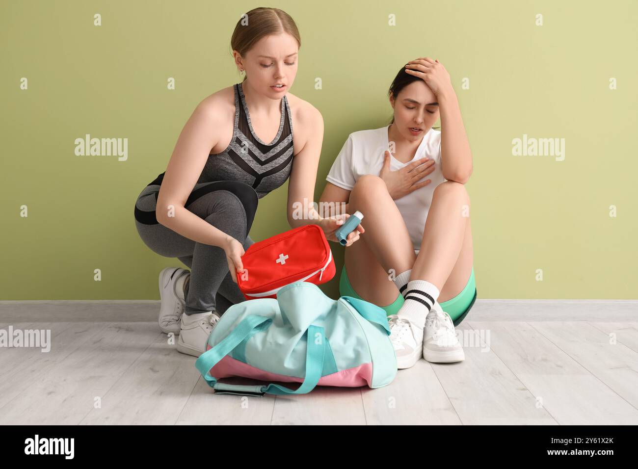 Female trainer with inhaler giving young woman first aid near green ...