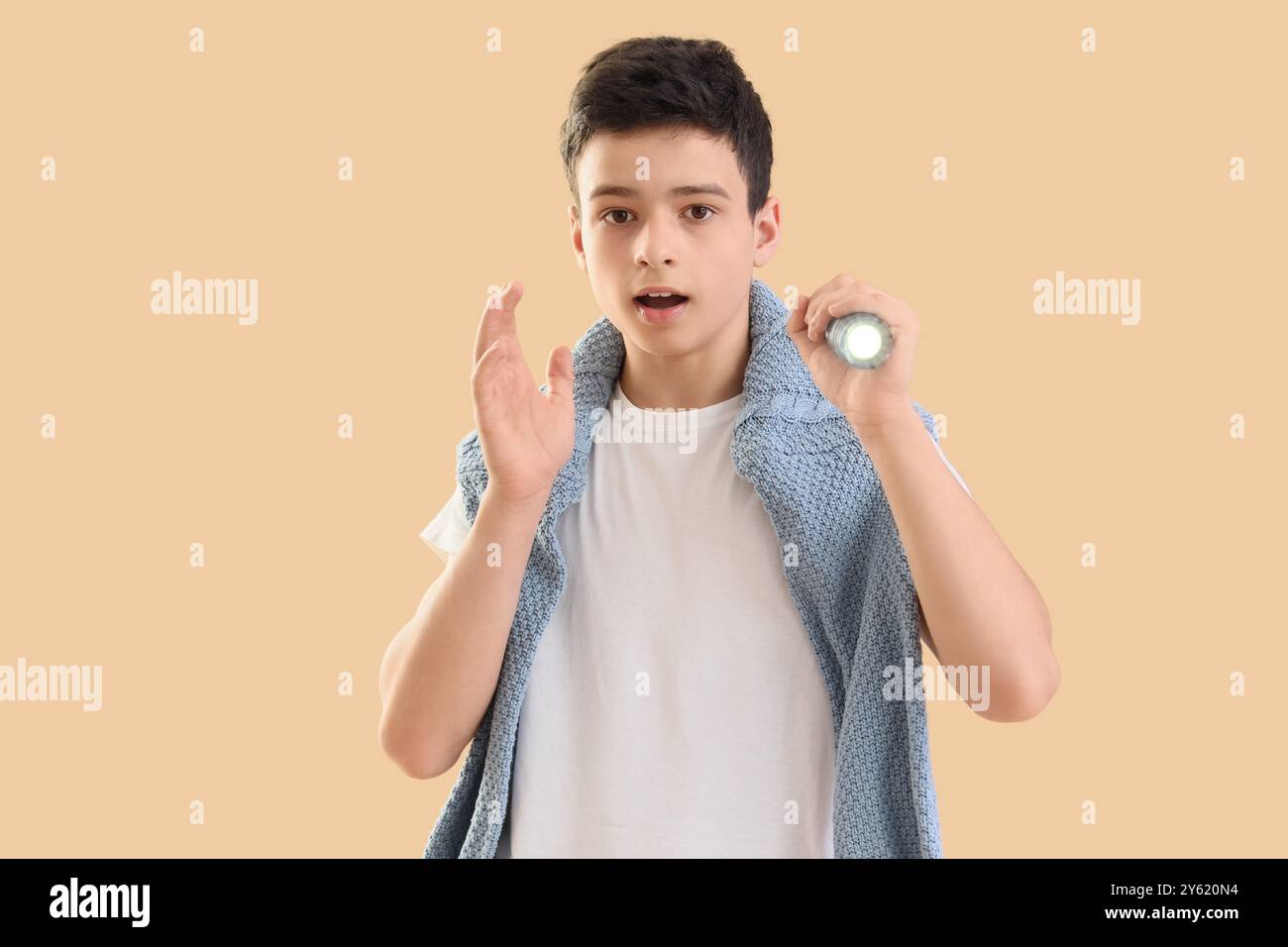 Shocked teenage boy with shining flashlight on beige background Stock ...