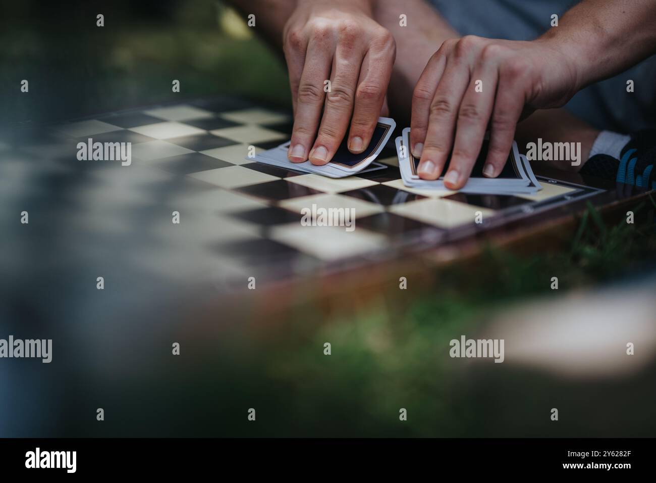 Hands shuffling playing cards on outdoor chess board setup Stock Photo ...