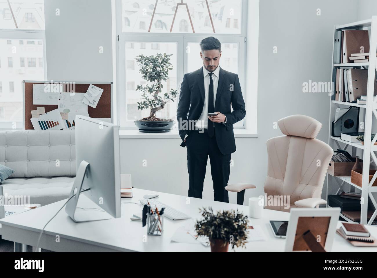 Texting to business partner. Good looking young man in full suit using ...