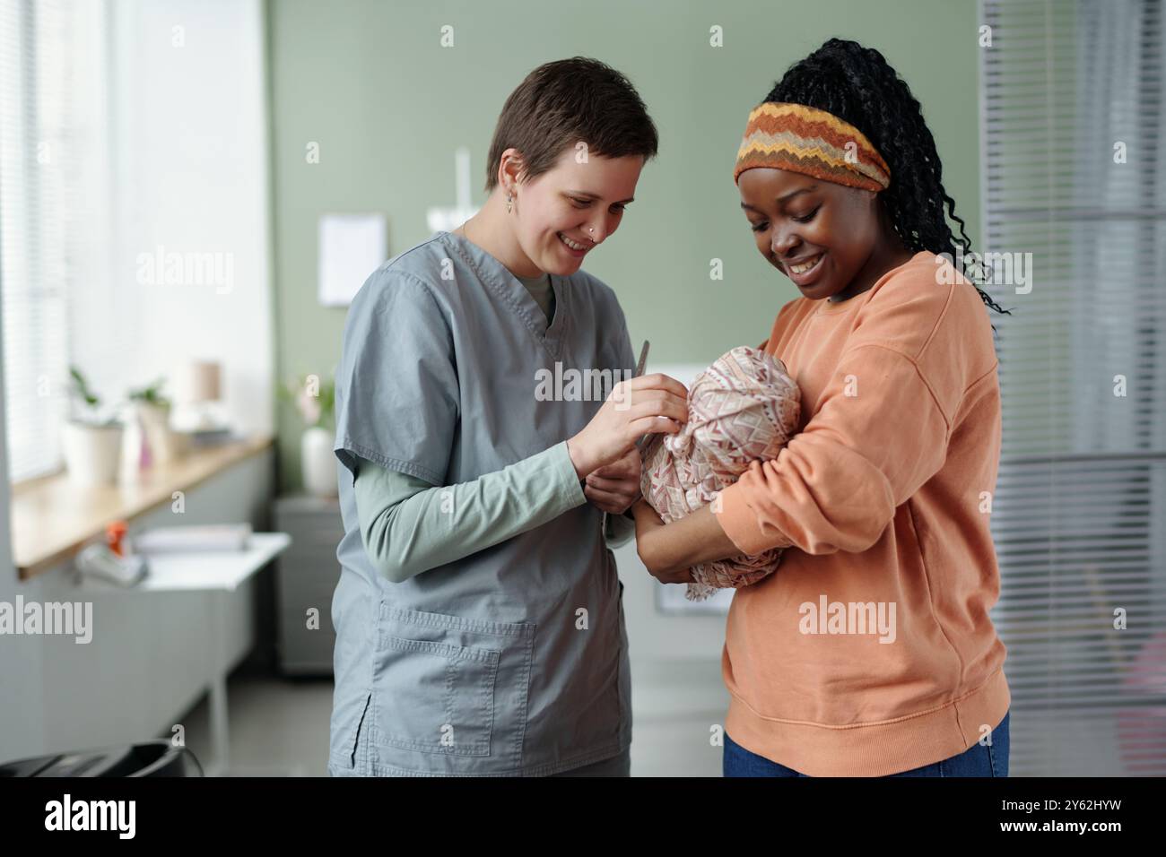 Nurse checking on newborn while mother holds infant close in hospital ...